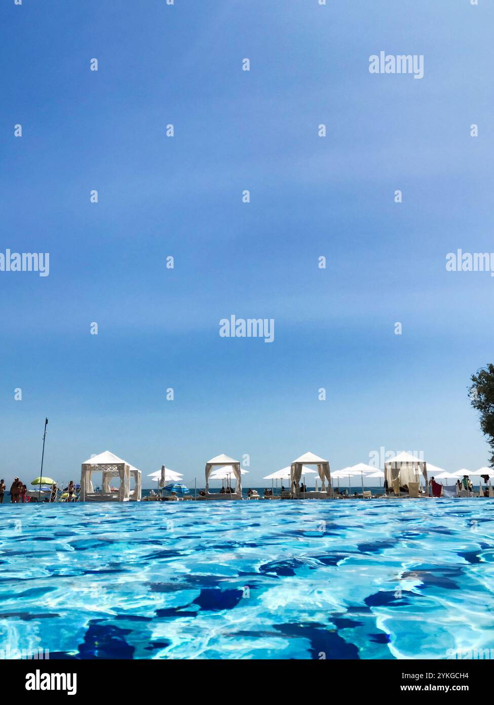 A vibrant blue swimming pool under a clear sky with inviting cabanas ...
