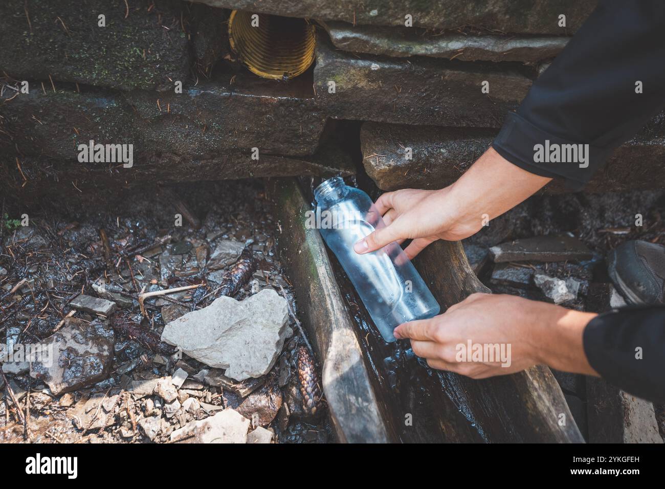 Filling a reusable water bottle from a natural spring in the forest. A ...