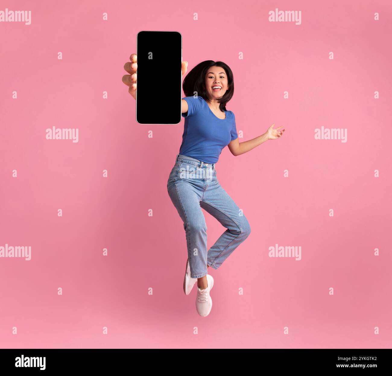 Asian woman jumping and showing blank smartphone screen for mockup ...
