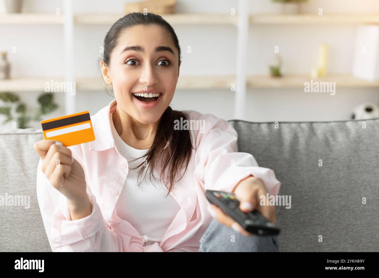 Excited woman holding remote control and debit credit card Stock Photo ...