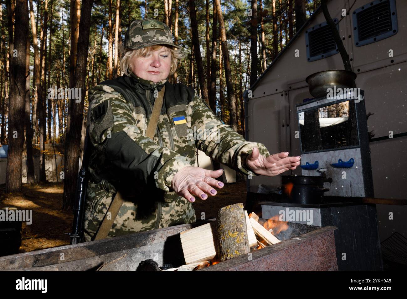 A woman in military uniform warms her hands by the fire during a ...