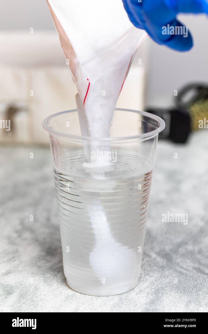 Gloved hands pouring glucose monohydrate powder into a plastic cup with ...