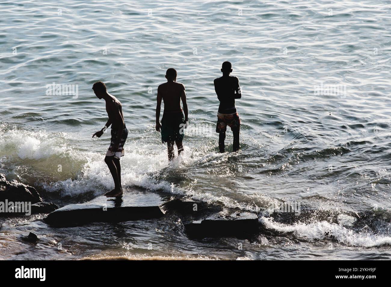Three young bathers are seen in silhouette at dusk on Barra beach on ...