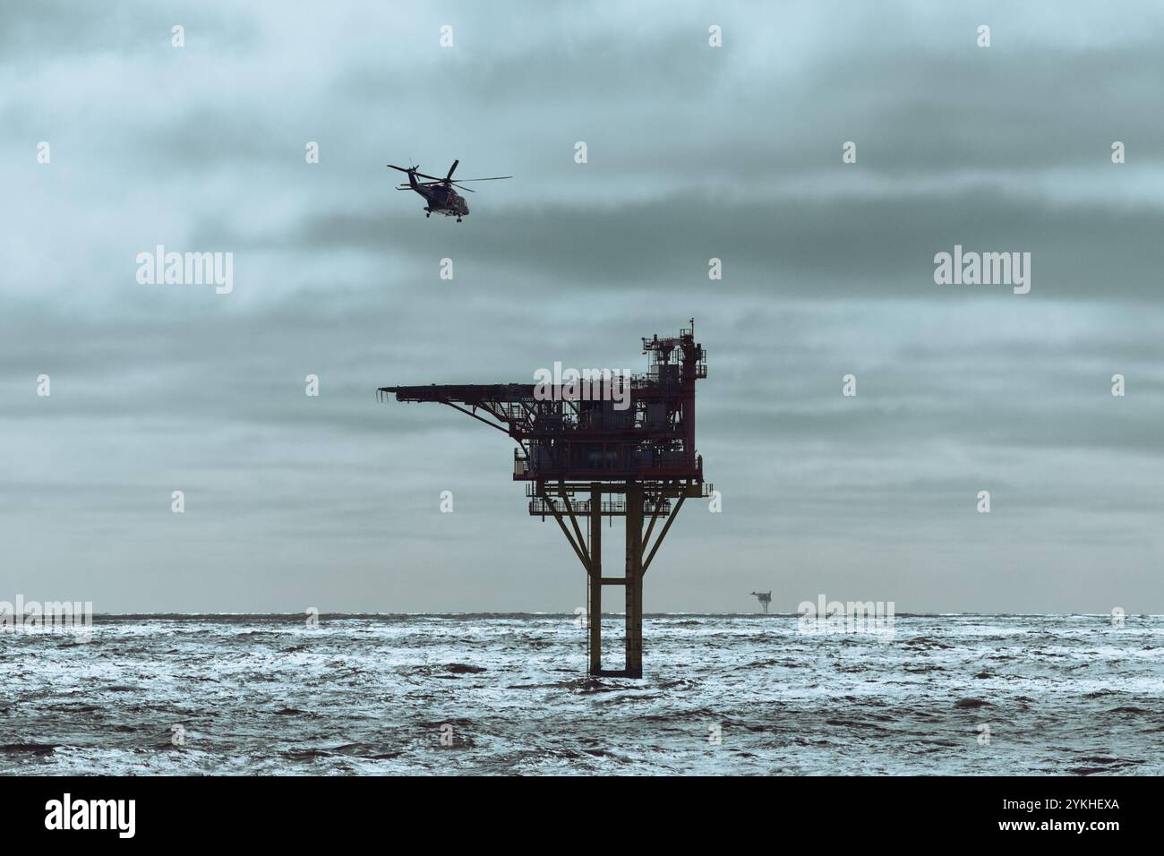 Helicopter flying towards offshore oil rig in the sea for landing, with ...