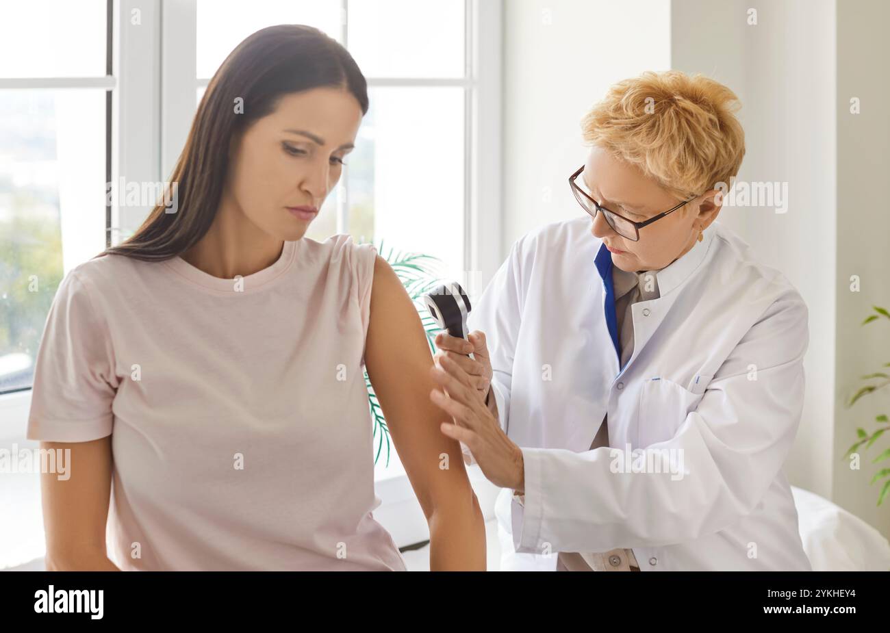 Doctor looking very closely at young woman arm skin with dermatoscope ...