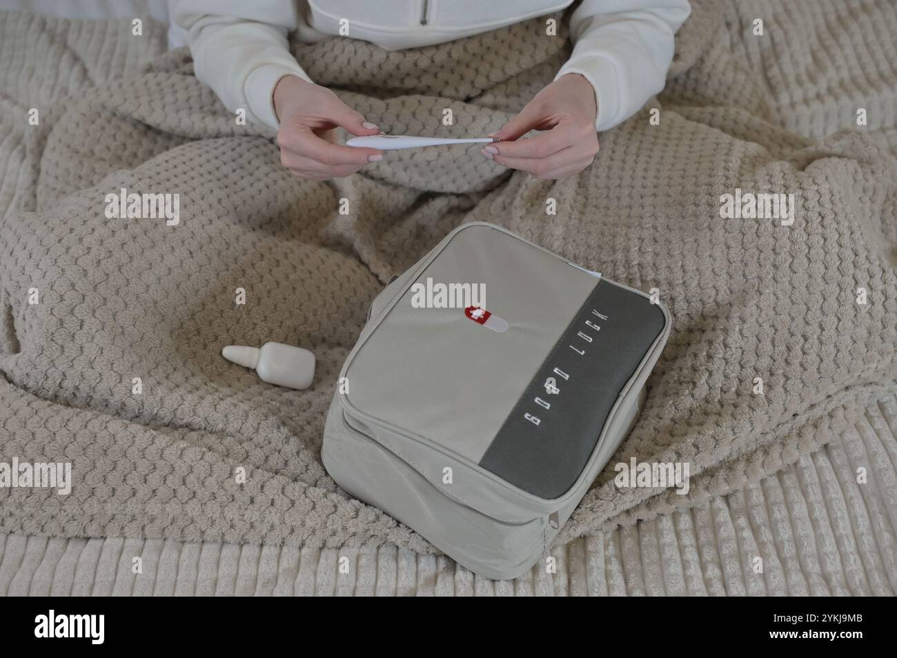 Woman holding thermometer, gray home first aid kit and nasal spray on ...