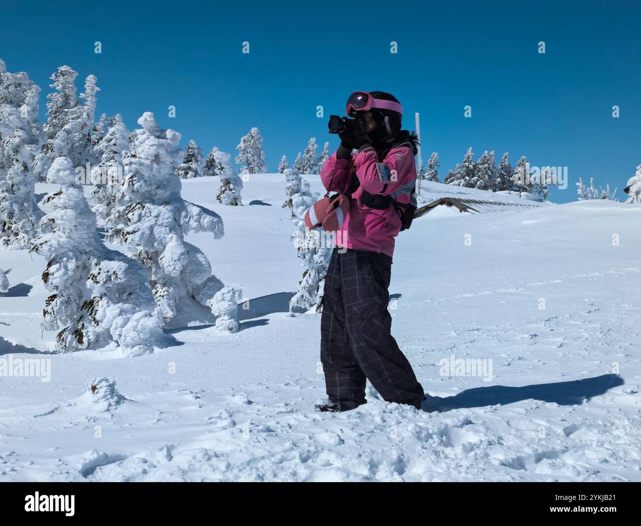 Female snowboarder photographing a frozen forest landscape on a clear ...
