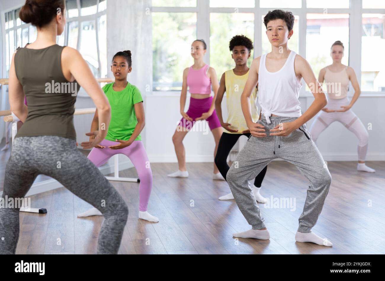 Thin teenage boy practicing plie position of ballet standing in row ...