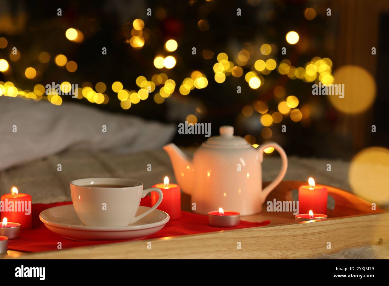 Aromatic tea in cup, teapot and burning candles on bed against blurred ...