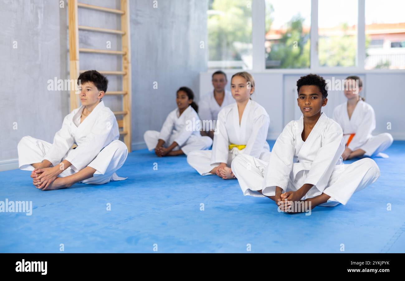 Group of multinational children in white kimono sits in butterfly pose ...