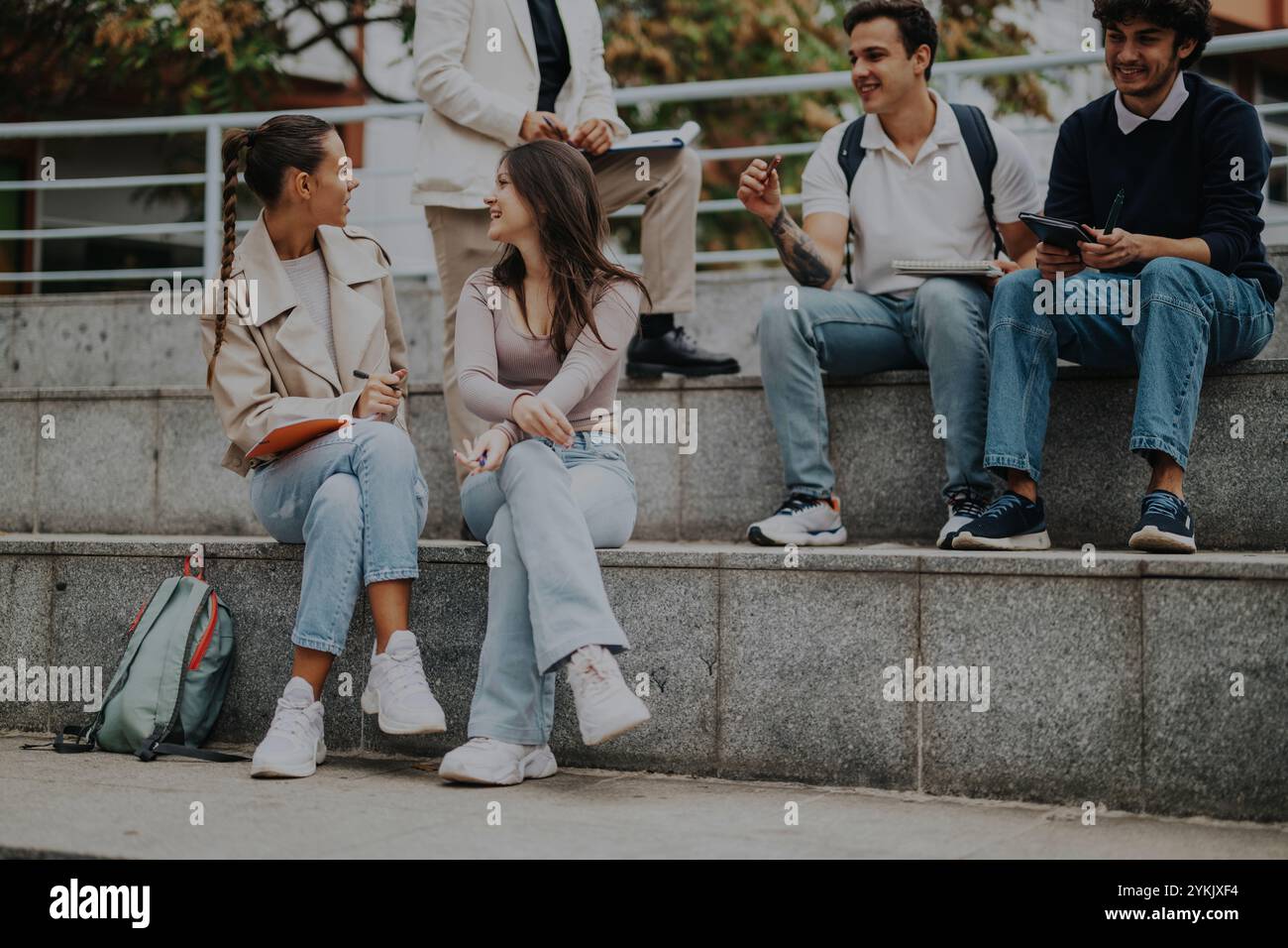 Group of students collaborating with professor outdoors on campus steps ...