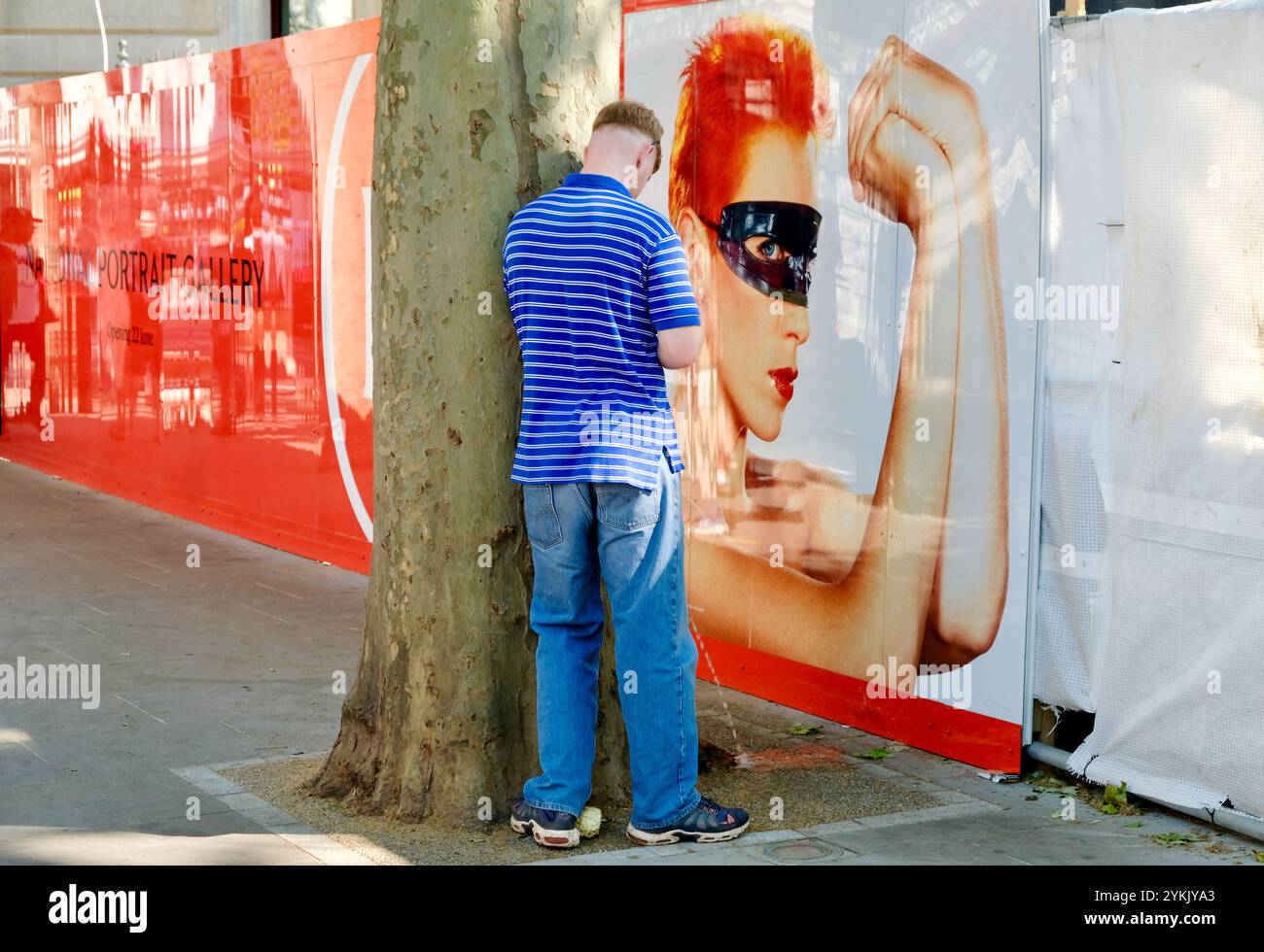 A man urinating behind a tree on Charing Cross Road beside a photo of ...