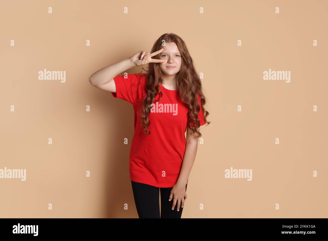 Cute teenage girl showing peace sign on beige background Stock Photo ...