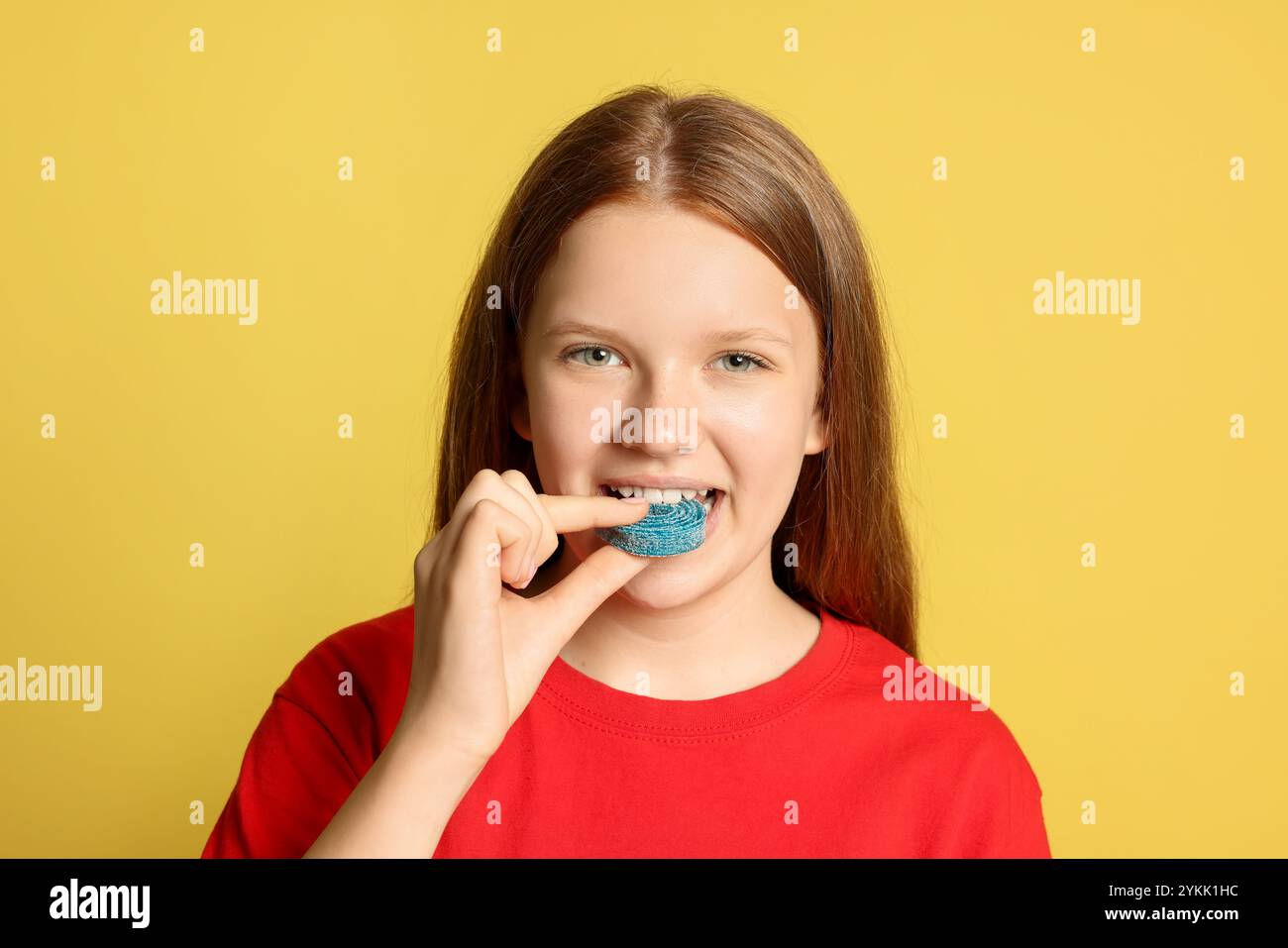 Teenage girl eating tasty gummy candy on yellow background Stock Photo ...