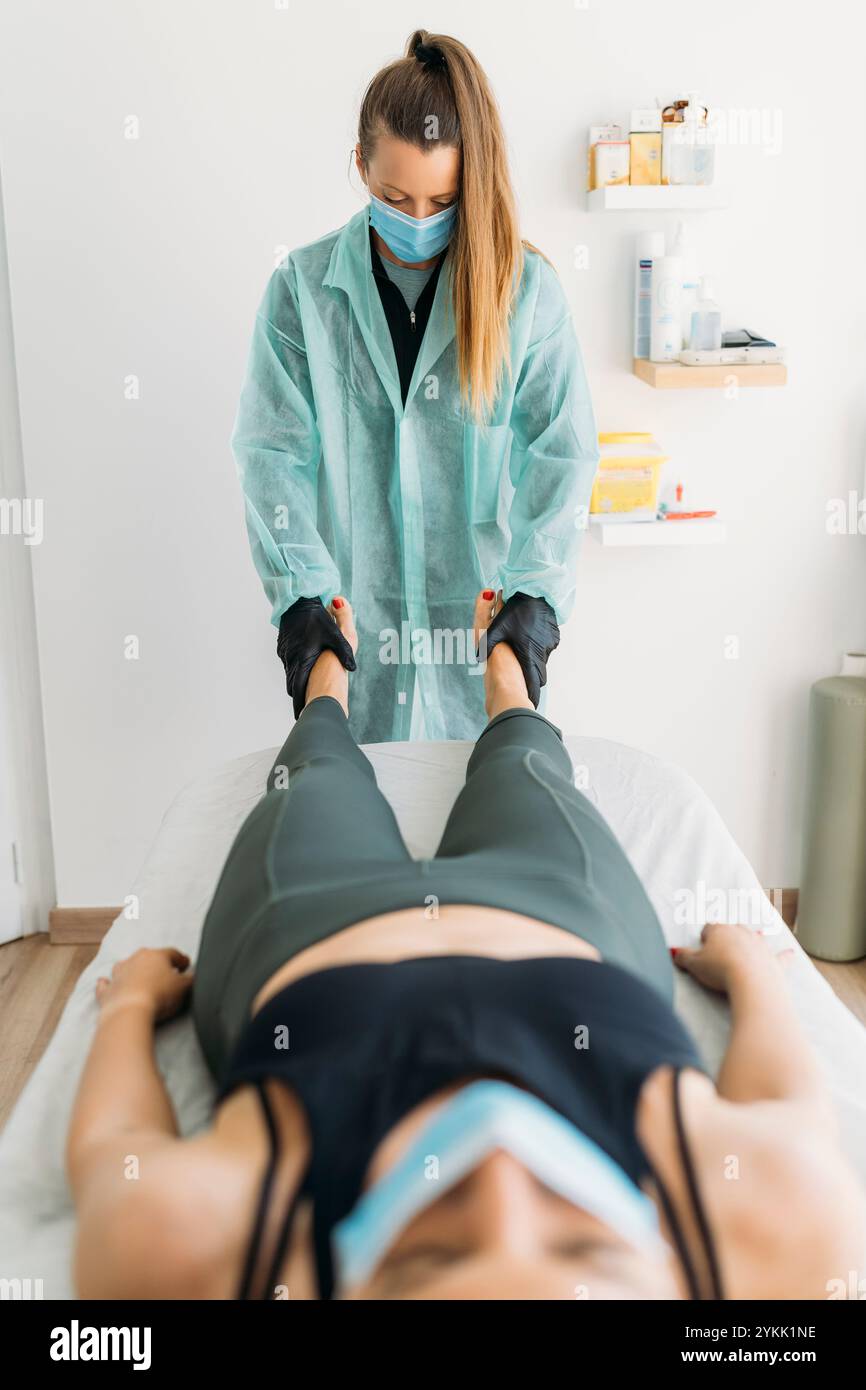 Physiotherapist stretching legs of woman lying on massage bed wearing ...