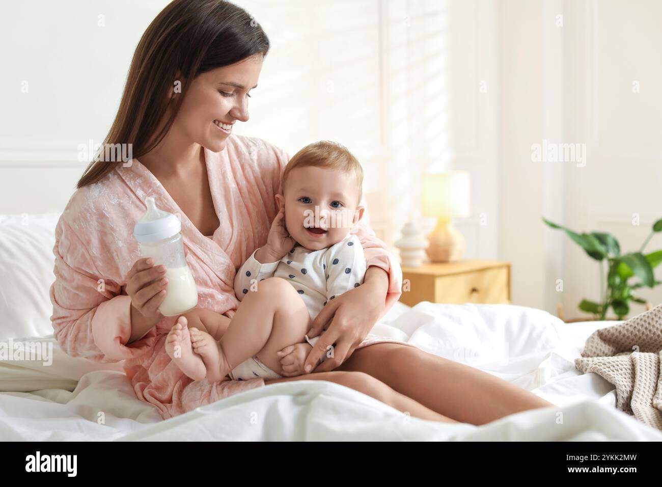Mother holding cute little baby and bottle of milk on bed at home. Space for text Stock Photo ...