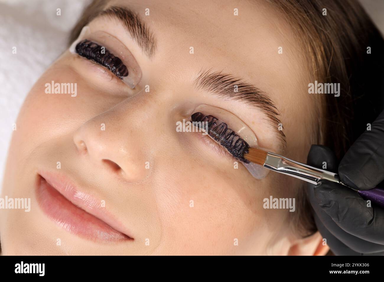 Eyelash lamination procedure. Esthetician applying dye on woman's ...