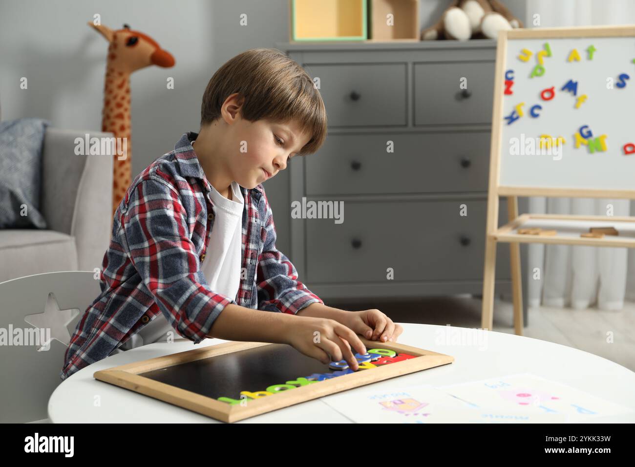 Little boy learning alphabet with magnetic letters at white table ...