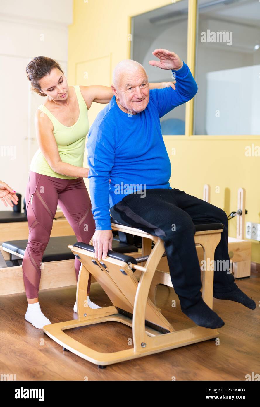 Elderly man practicing Pilates system on reformer supervised by ...