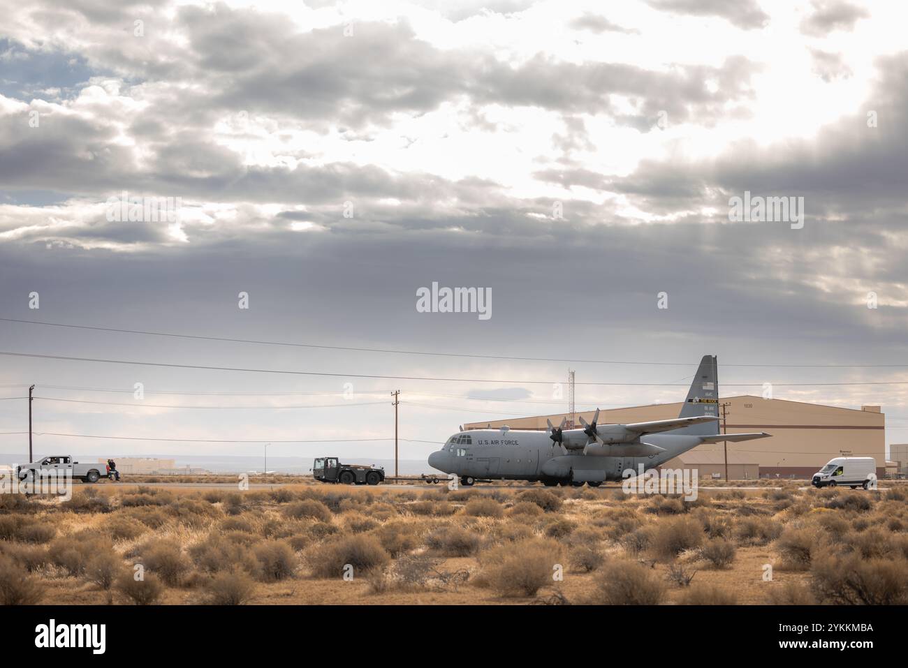 Crews carefully tow a C-130E aircraft down a road at Edwards Air Force ...