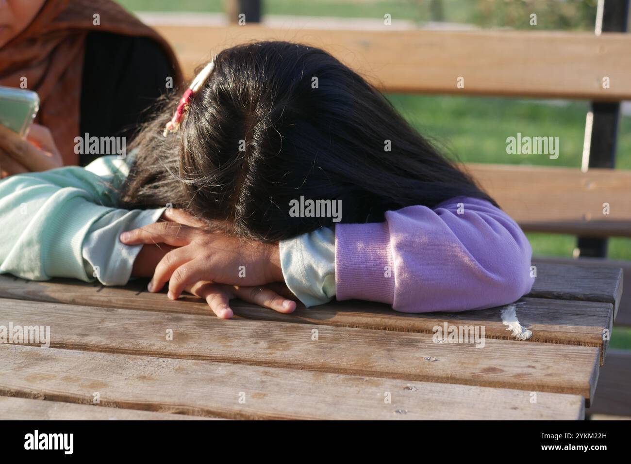 A child sitting outdoors with their head resting in their hands ...