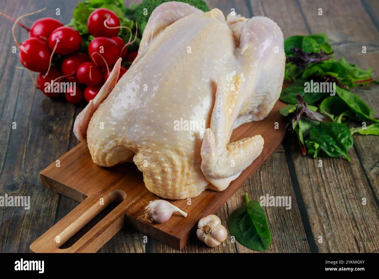Fresh whole chicken prepared for cooking alongside vegetables and ...