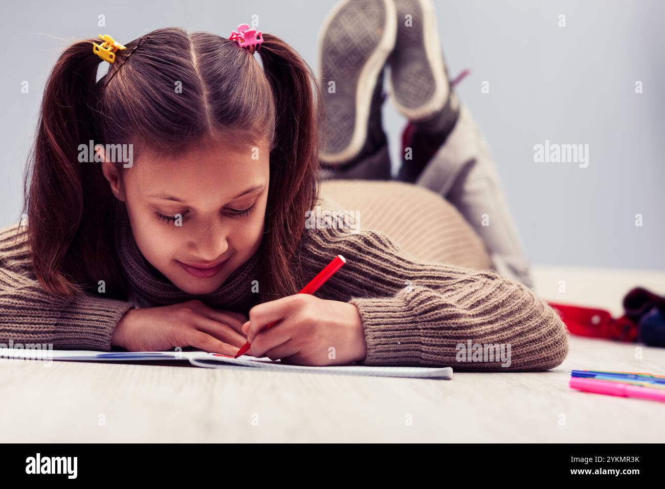 Young girl with pigtails is lying on her stomach on the floor ...