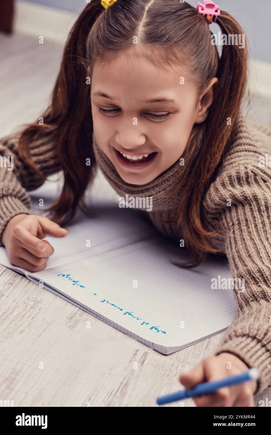 Happy elementary school girl writes in her notebook at home, smiling ...