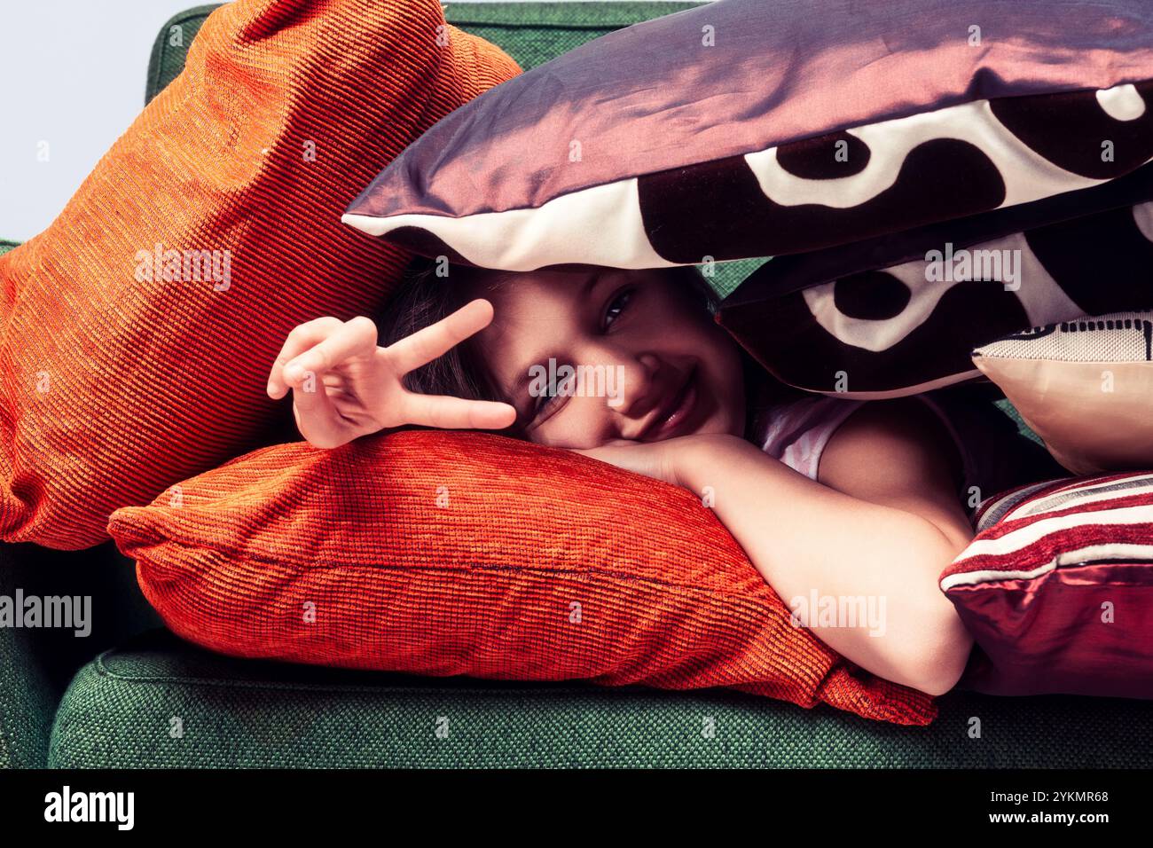 Smiling child is comfortably lying on a sofa, hiding under a pile of ...