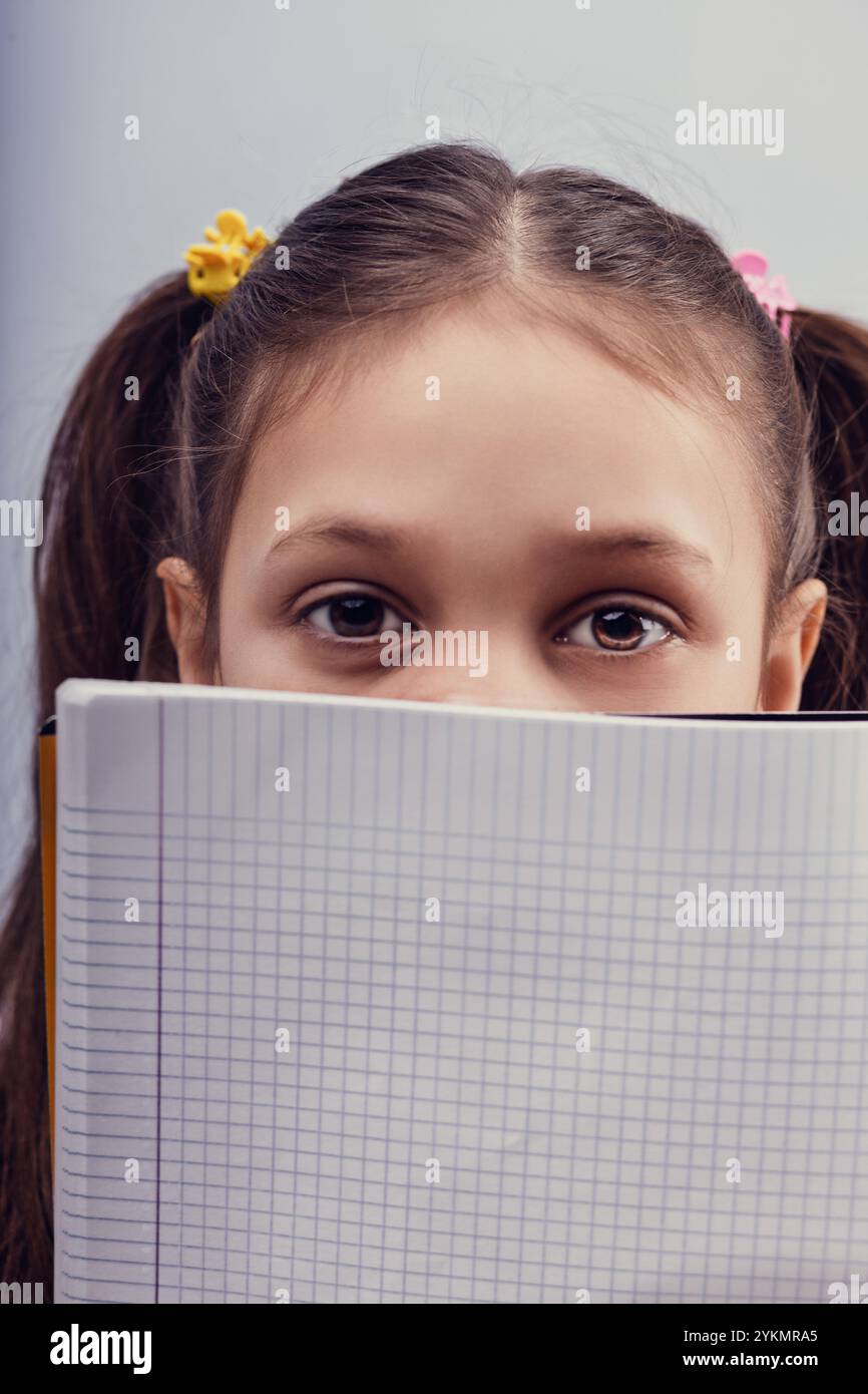 Elementary school girl with two ponytails is peering over a graph paper ...