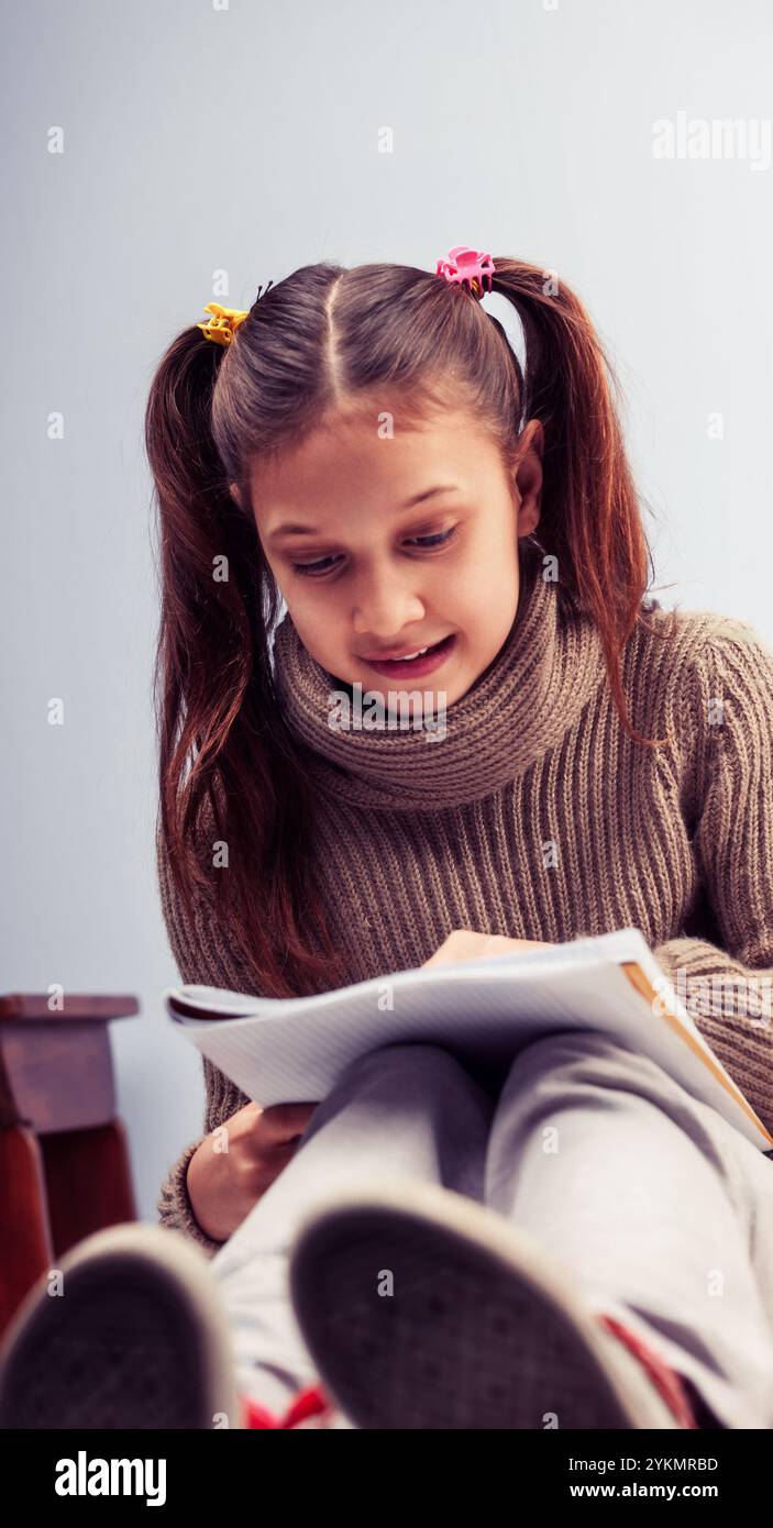 Focused girl, 8-9 years old, reads a book while doing homework ...