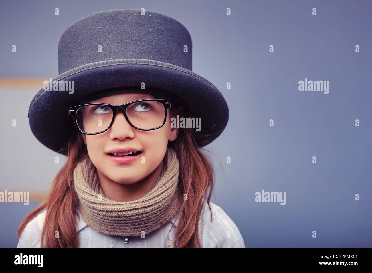 Curious girl in a top hat and glasses gazes up playfully against a ...