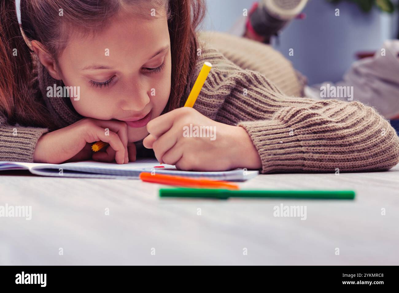 Young girl is lying on her stomach on the floor, diligently drawing ...