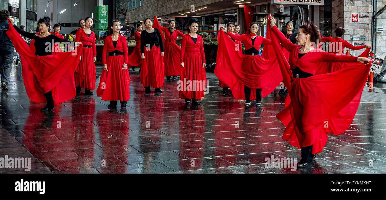 Group of women dancing gracefully in vibrant red dresses at a public ...
