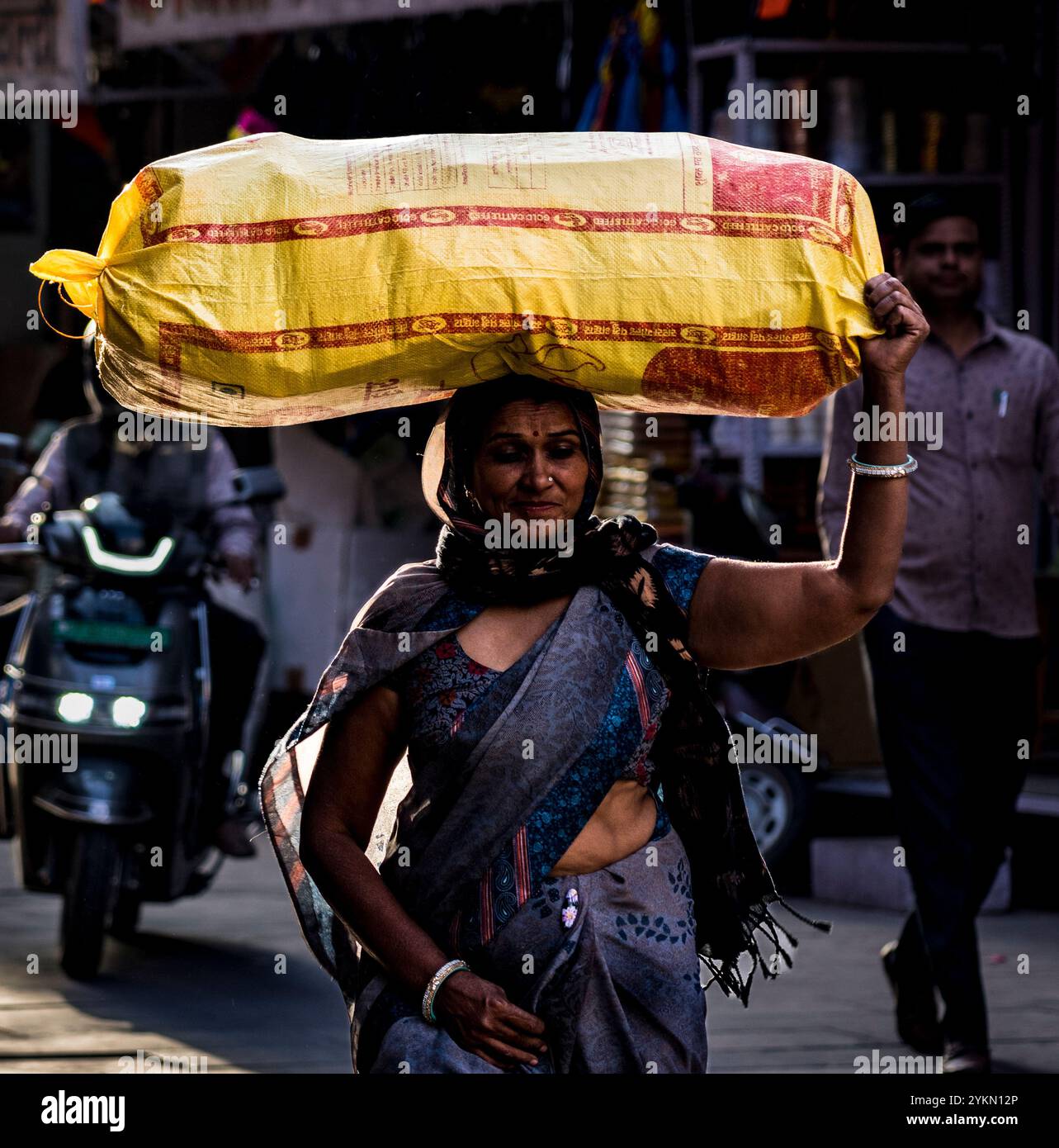 Woman in traditional attire balances a bright cloth bundle on her head ...