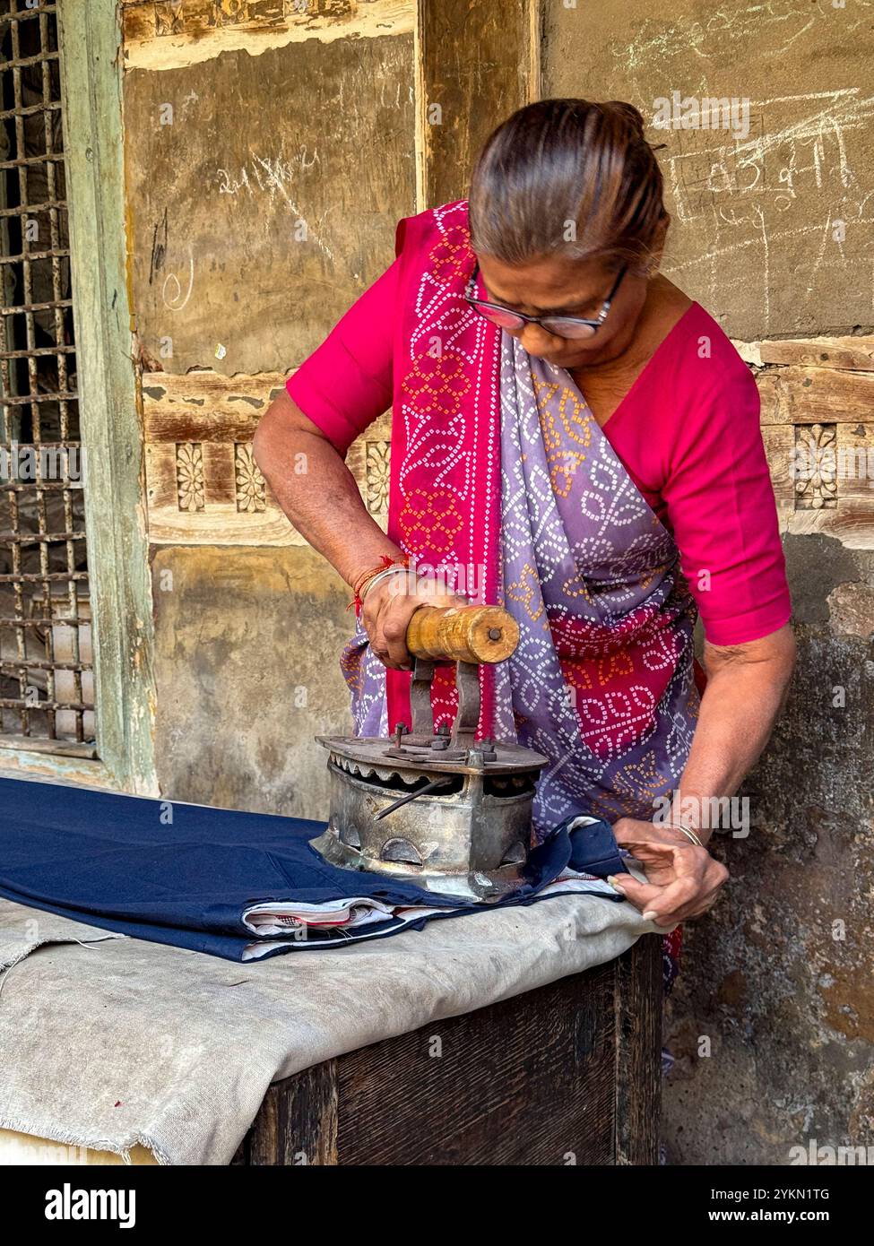 Indian woman in vibrant attire manually irons clothes with an antique ...