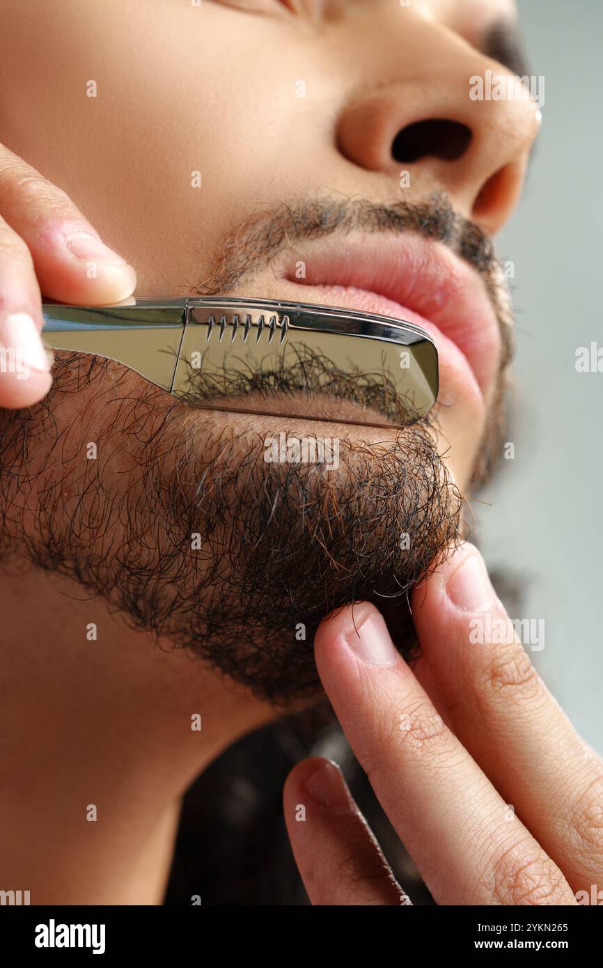 Man with curly hair grooming his beard carefully using a straight razor ...