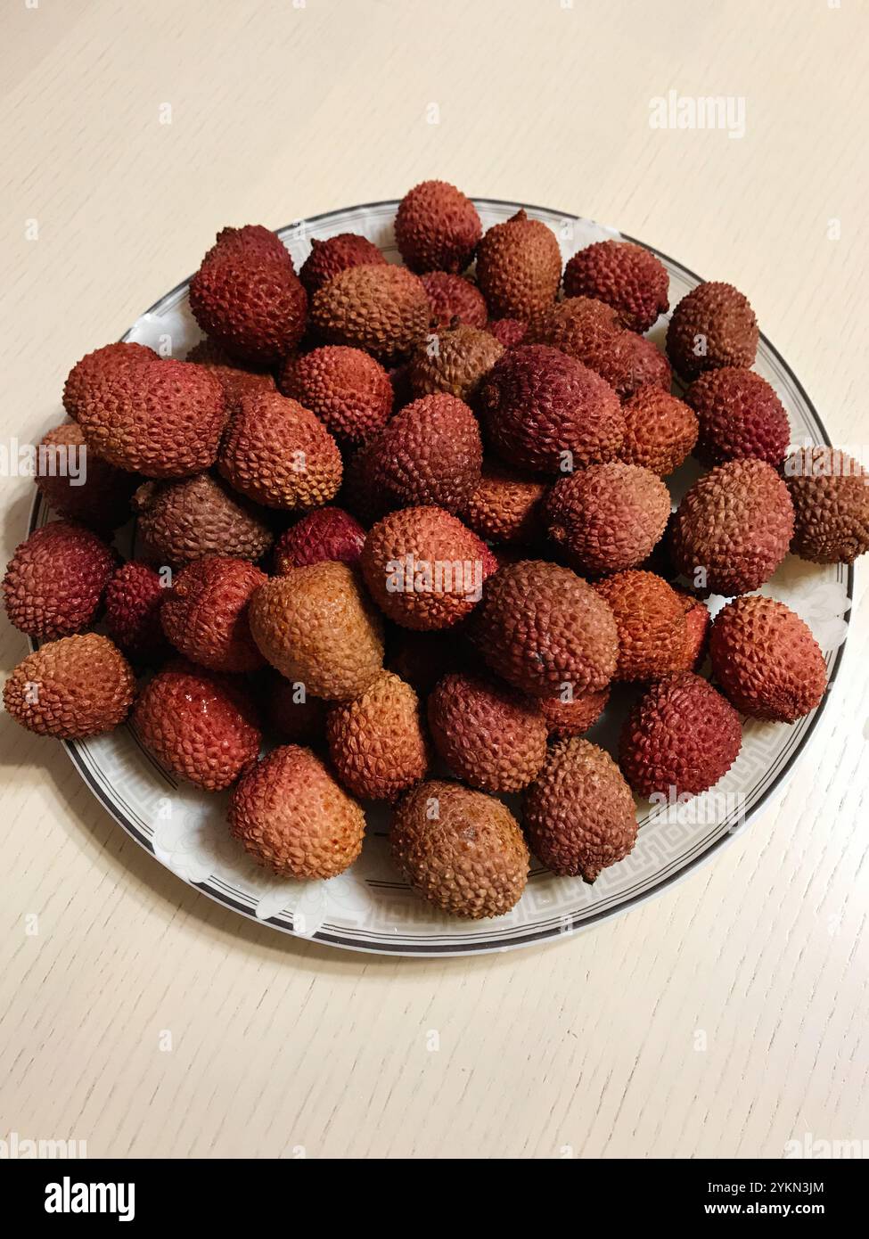 A collection of fresh lychee fruits piled on a patterned plate. The ...