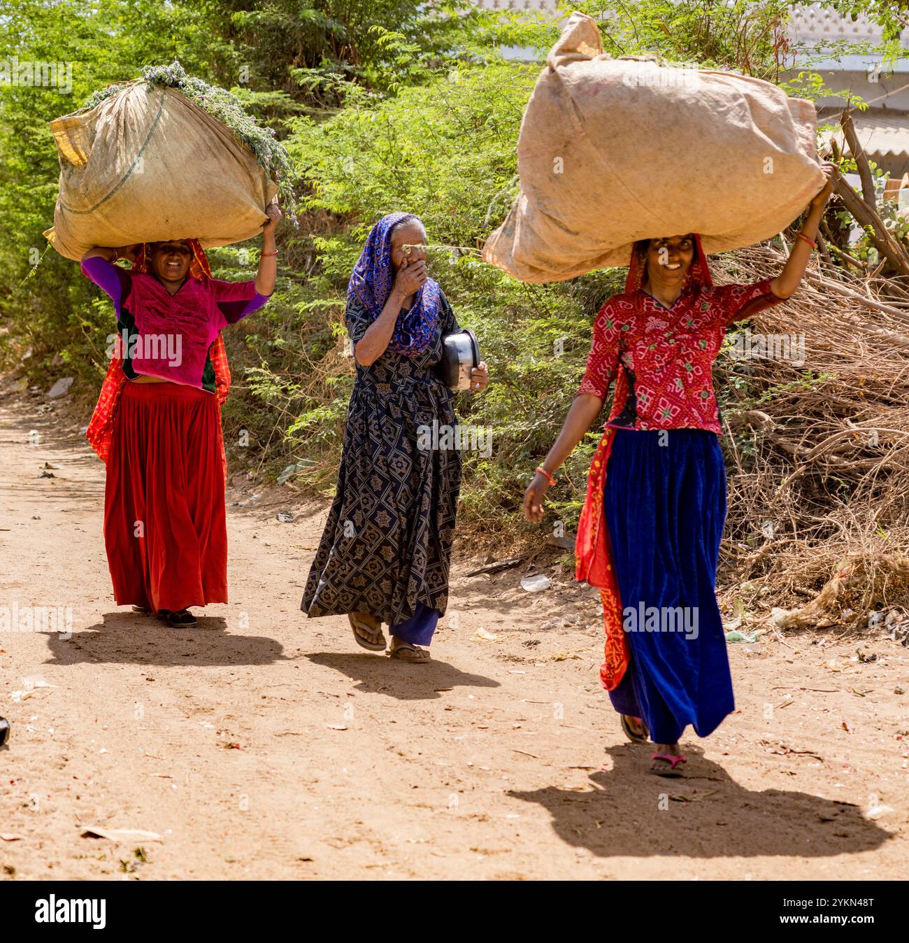 Three women balance large sacks on their heads while walking along a ...