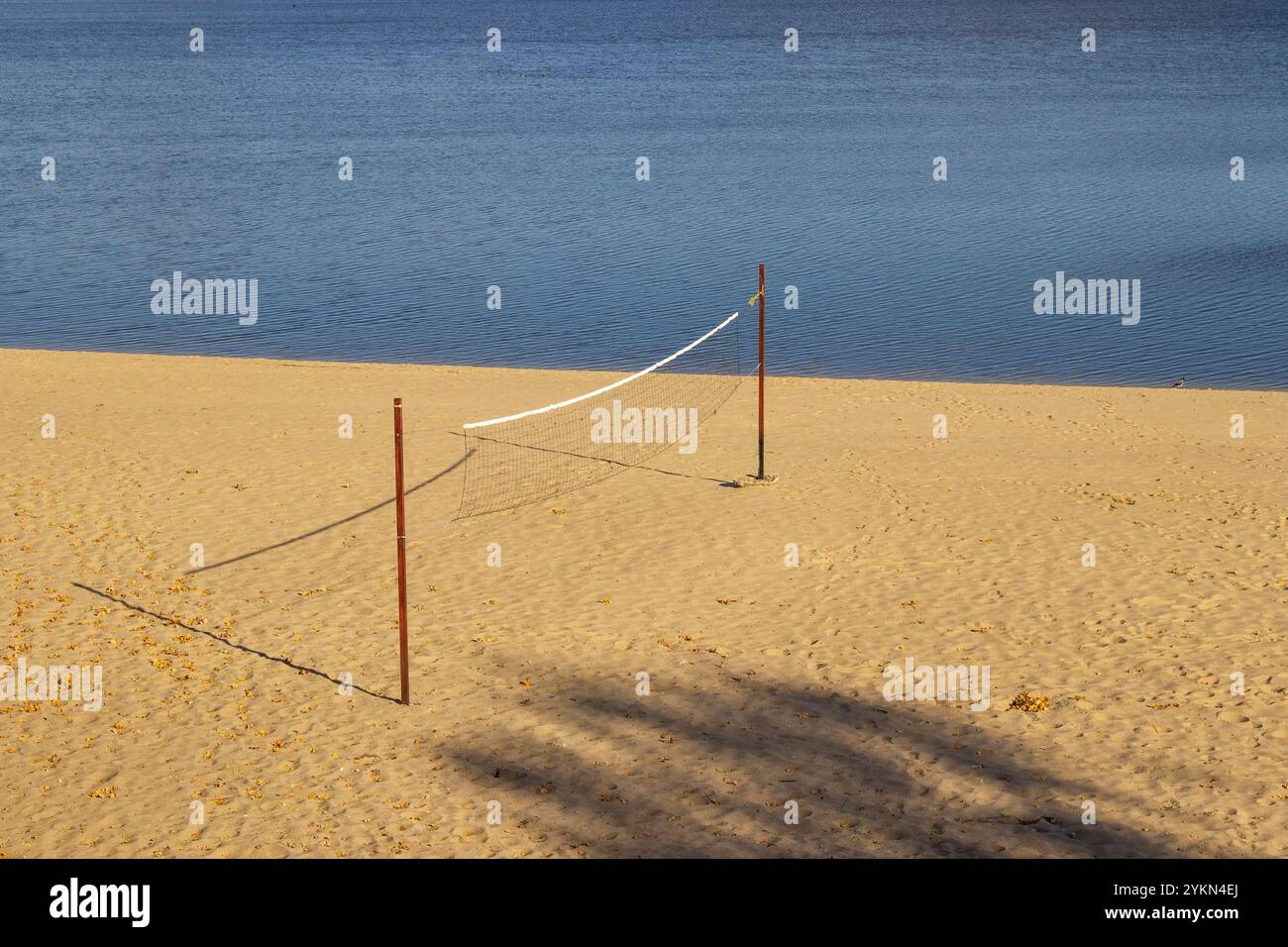 Volleyball net on an empty beach. Yellow sand and blue water, shadows ...