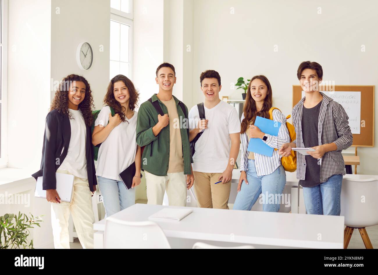 Group of a happy school or college students standing together in classroom and looking at camera ...