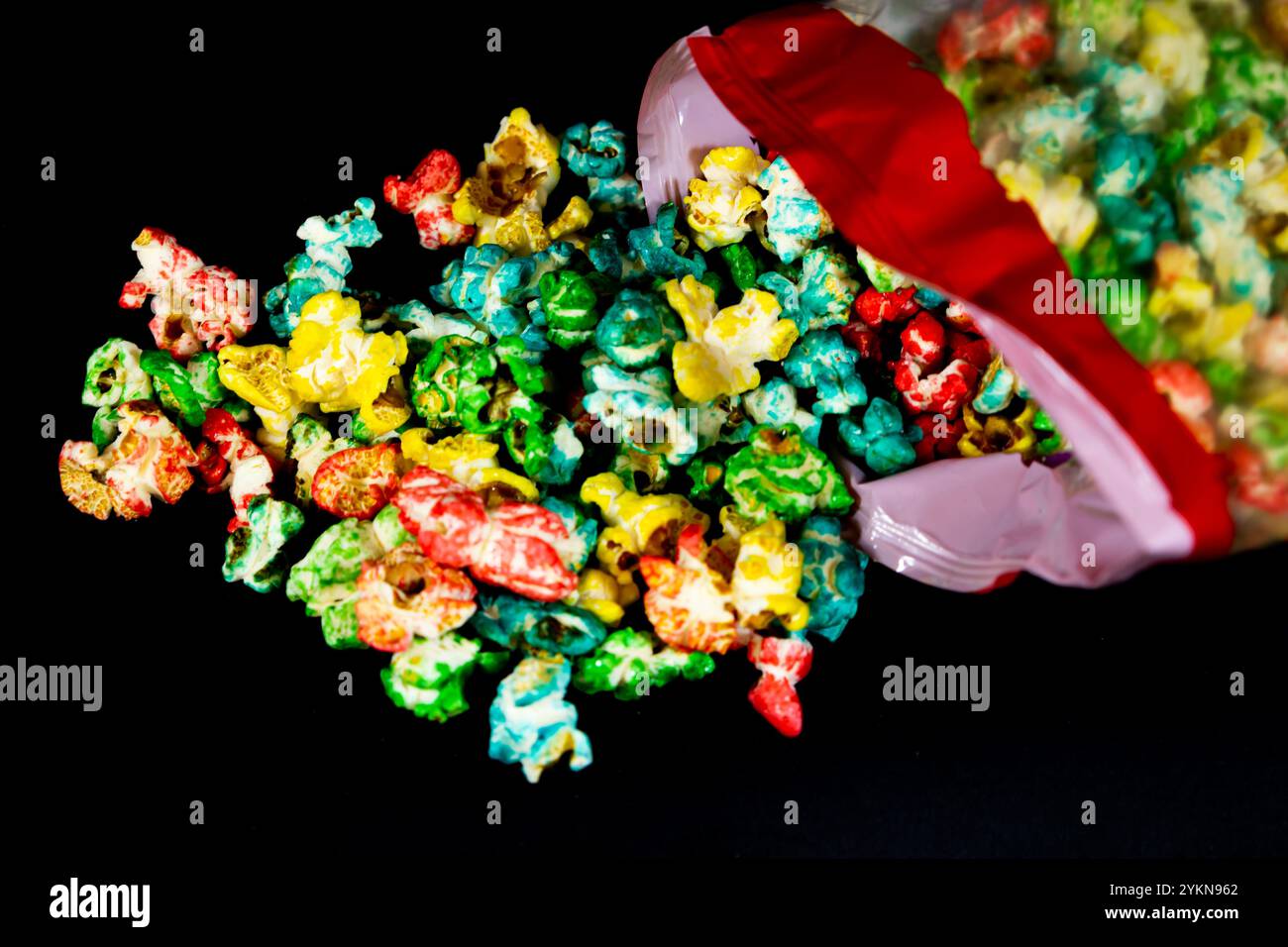 Fallen package with scattered colorful popcorn on a black background ...