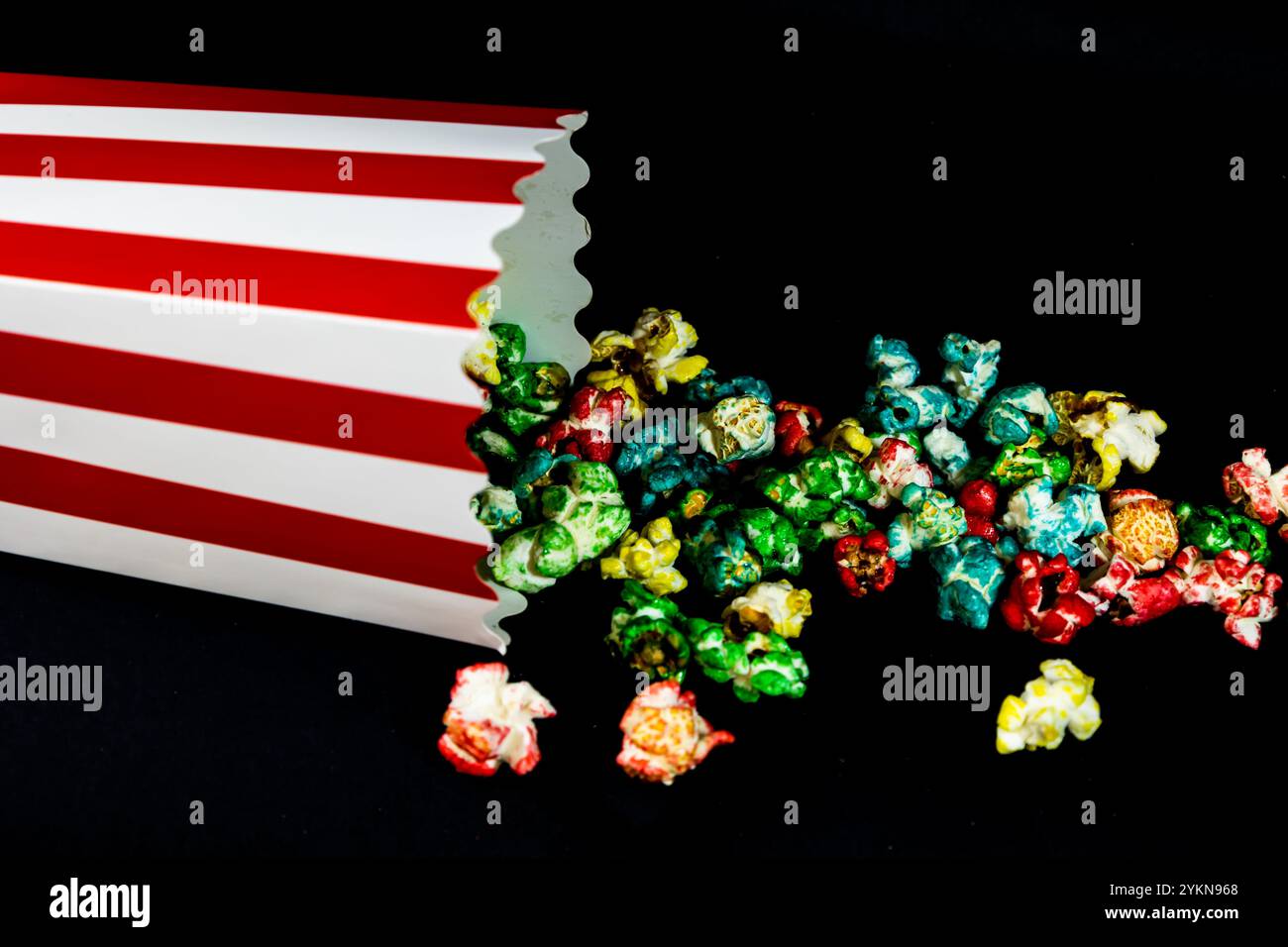 Fallen cardboard bucket with scattered colorful popcorn on a black ...