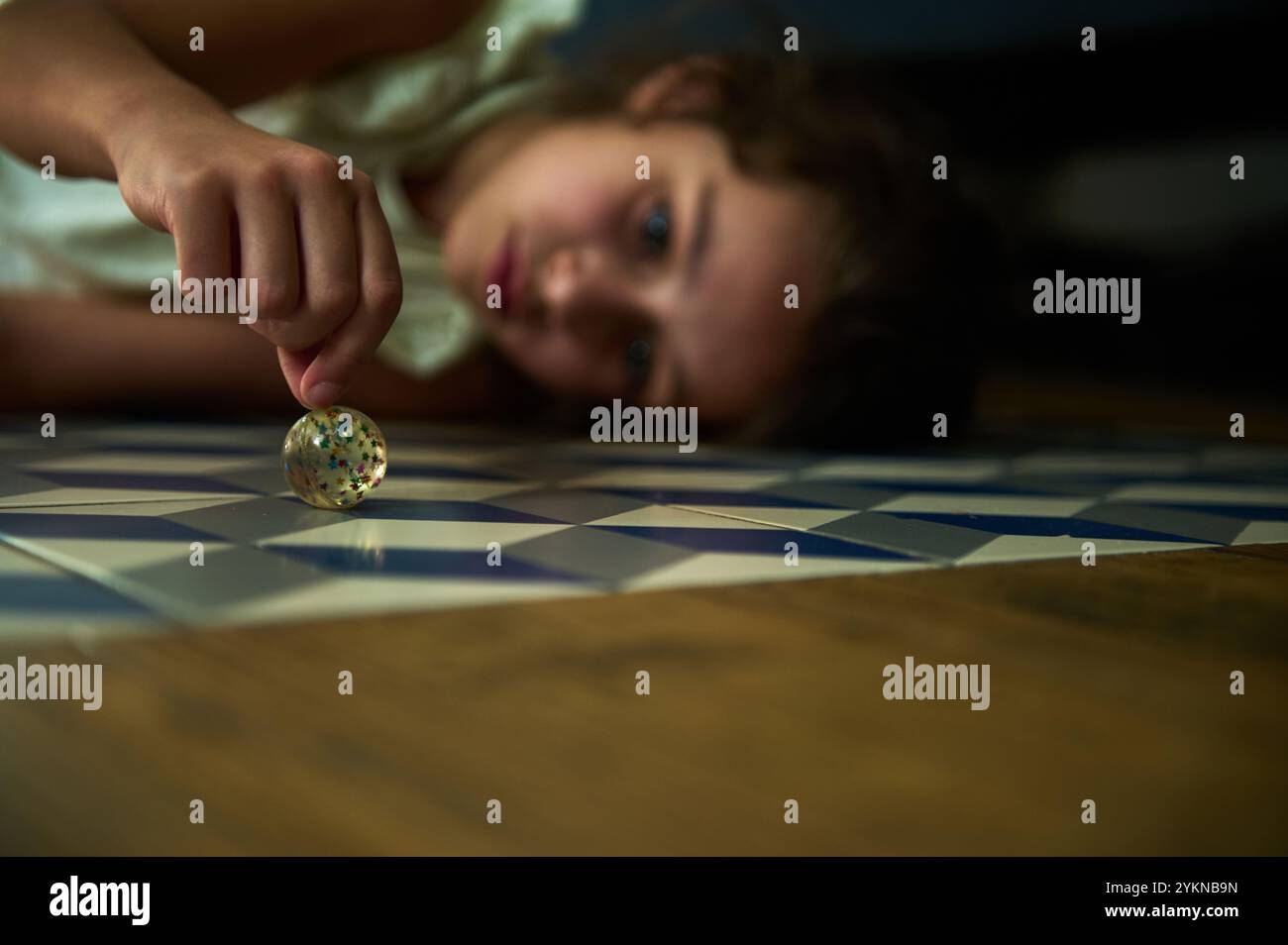 A child lies on a patterned tiled floor, intently observing a colorful ...