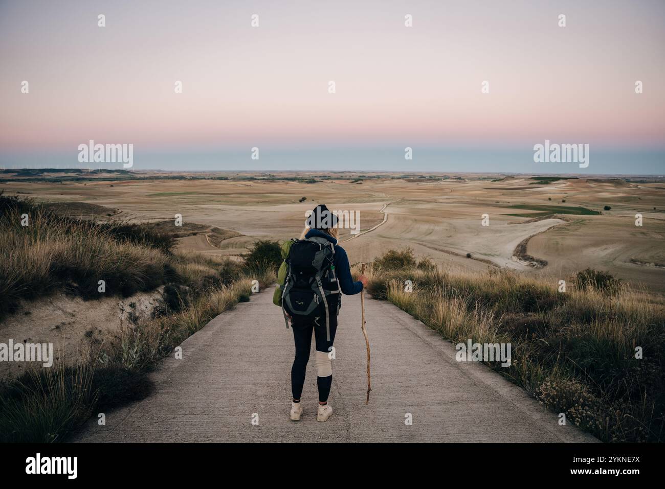 Pilgrim with hat and stick walking a road between a mountain and a ...