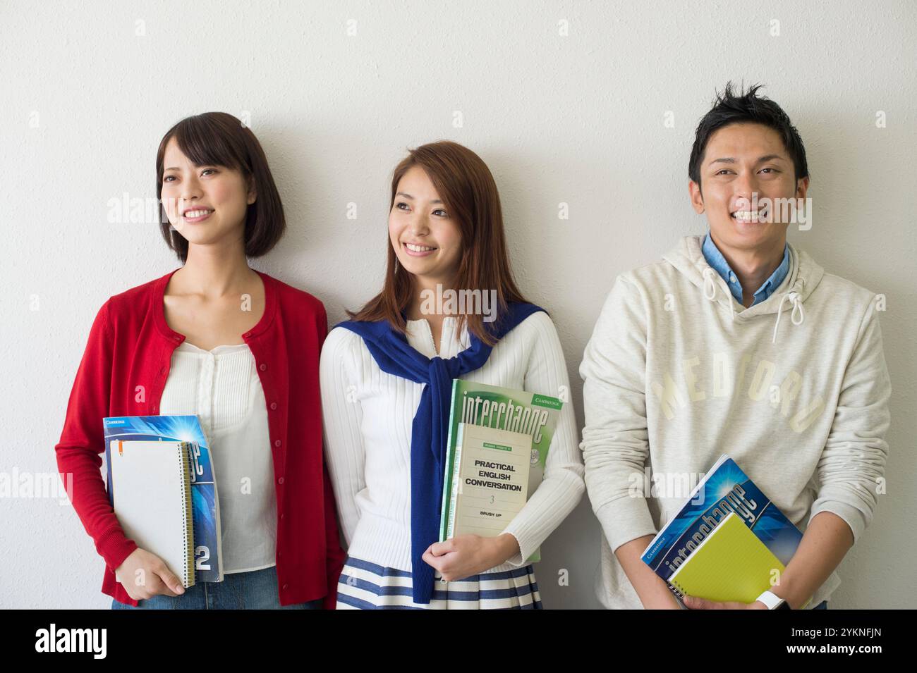 Three university students, male and female, standing with textbooks ...
