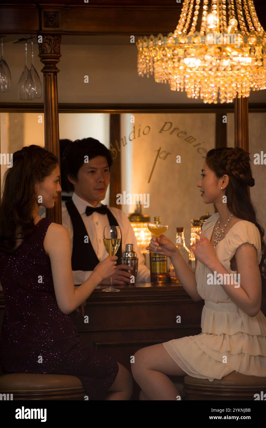Two female customers drinking cocktails with barman Stock Photo - Alamy