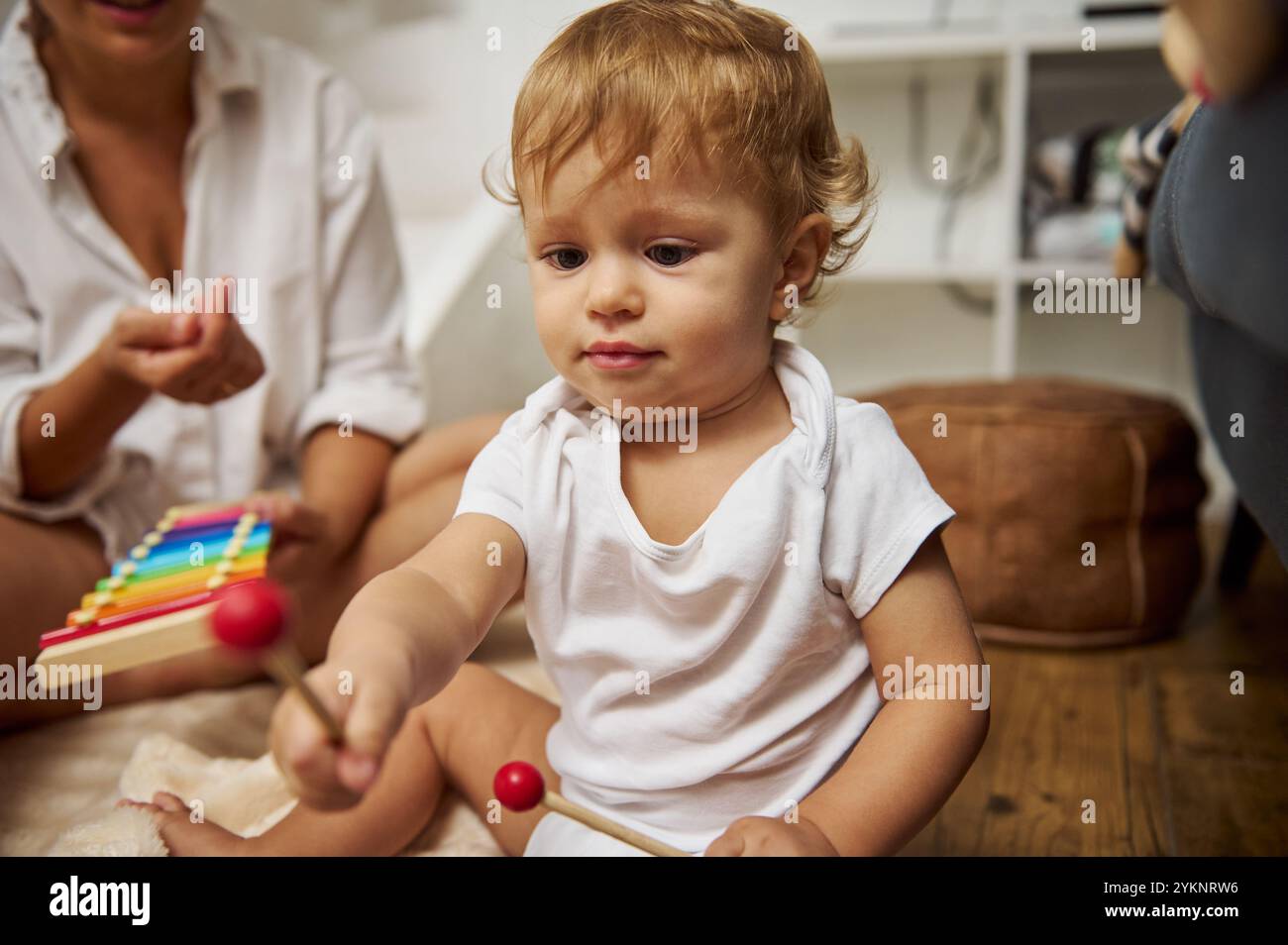 A young child plays a vibrant xylophone while sitting on the floor ...