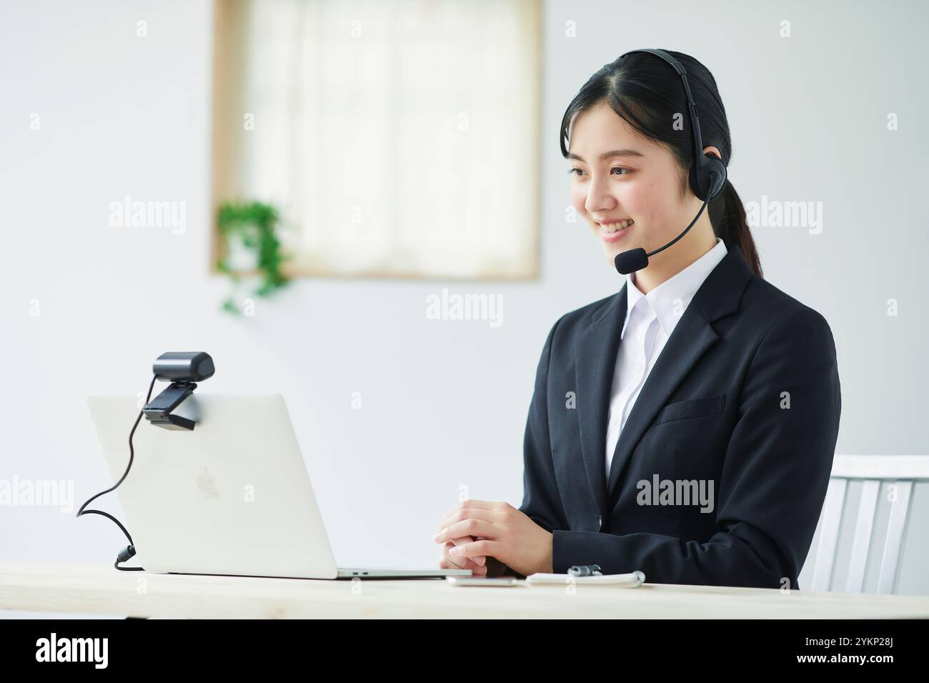 Young woman in smiling suit with intercom speaking into laptop camera ...