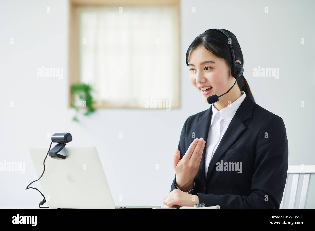 Young woman in smiling suit with intercom speaking into laptop camera ...